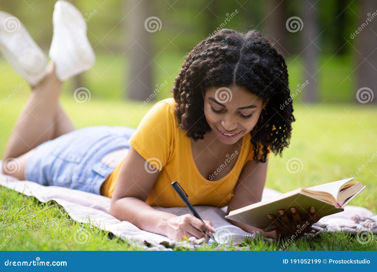 Black Female Student Taking Notes from Textbook on Picnic Blanket in ...