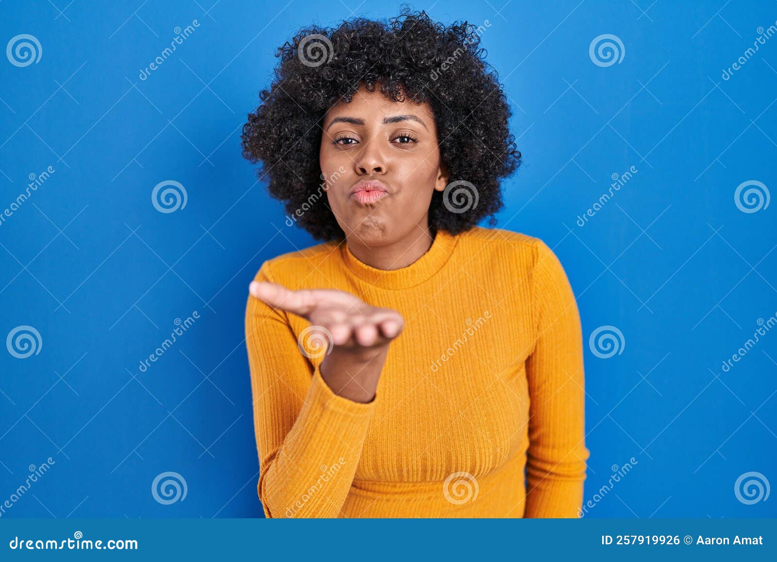 Black Woman With Curly Hair Standing Over Blue Background Looking At