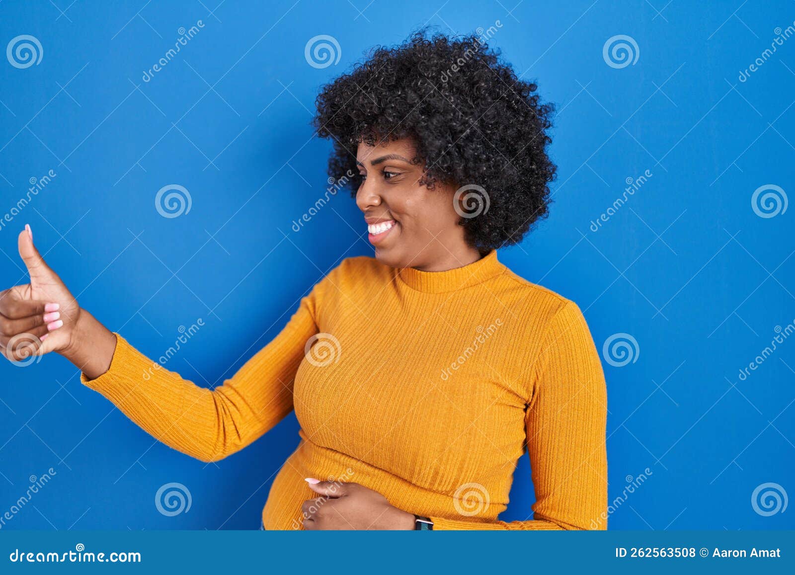 Black Woman With Curly Hair Standing Over Blue Background Looking Proud
