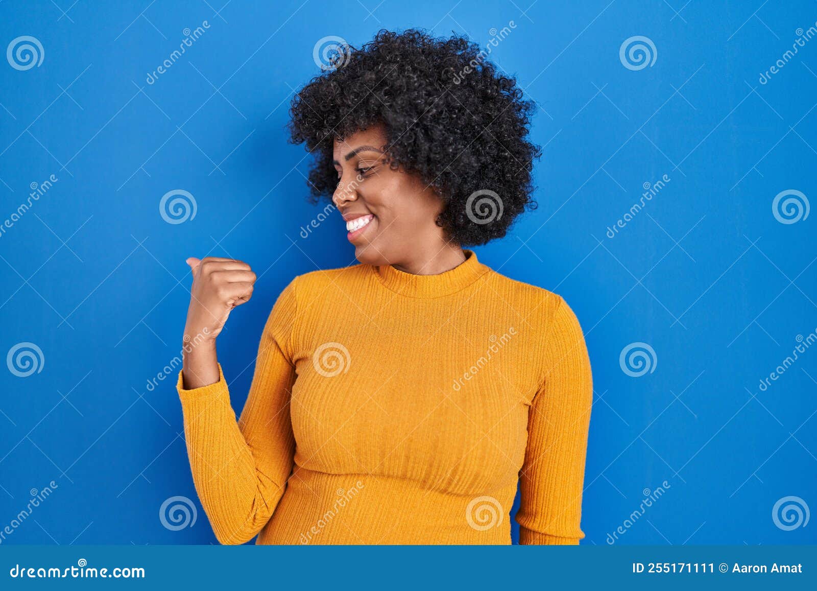 Black Woman With Curly Hair Standing Over Blue Background Smiling With