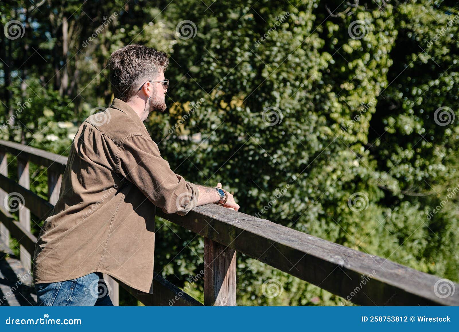 Blond Guy Leaning on the Railing of a Bridge in a Forest Looking ...