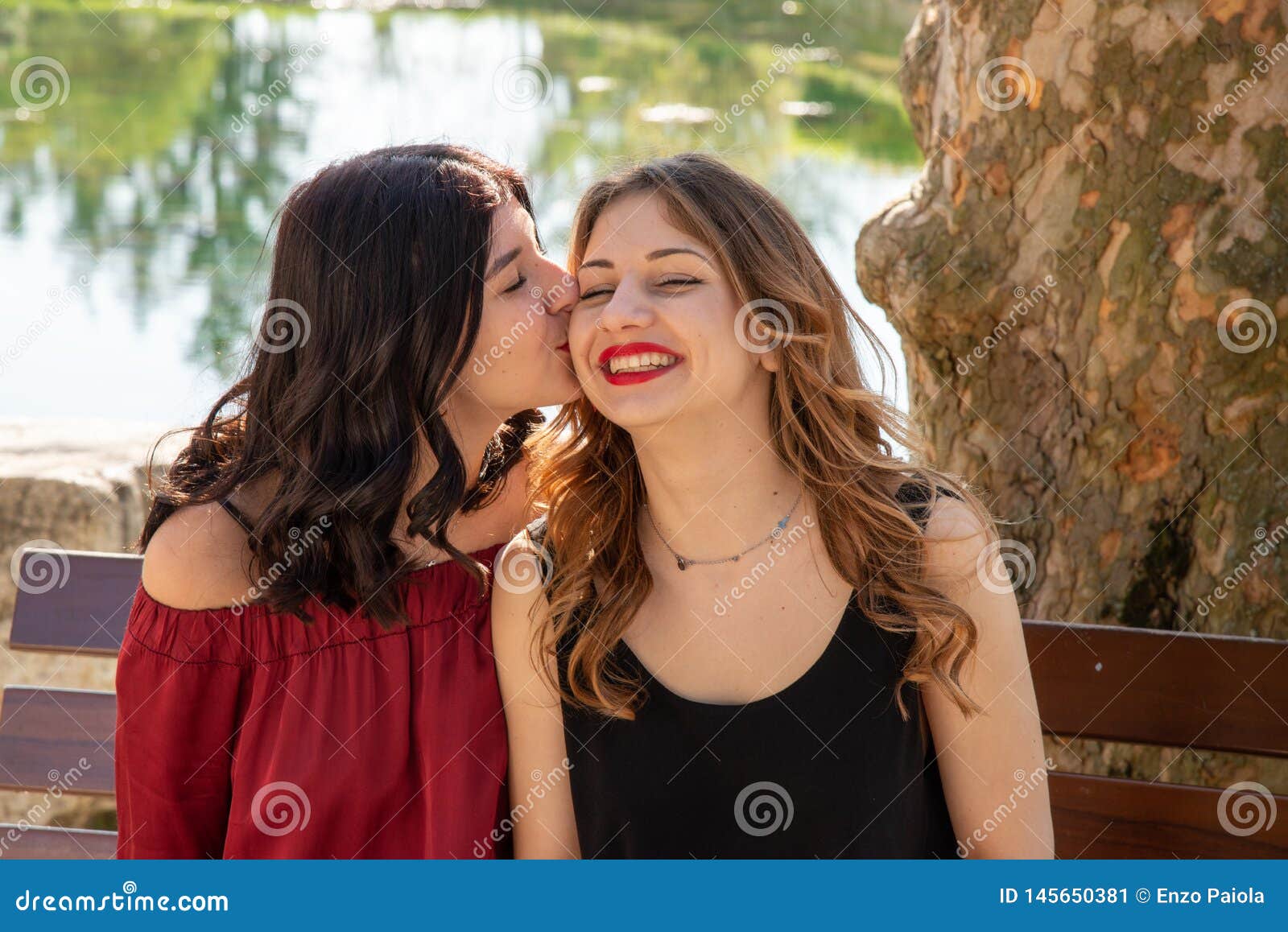 Close Up Of Two Friends Sitting On A Bench By A Lake Stock Image