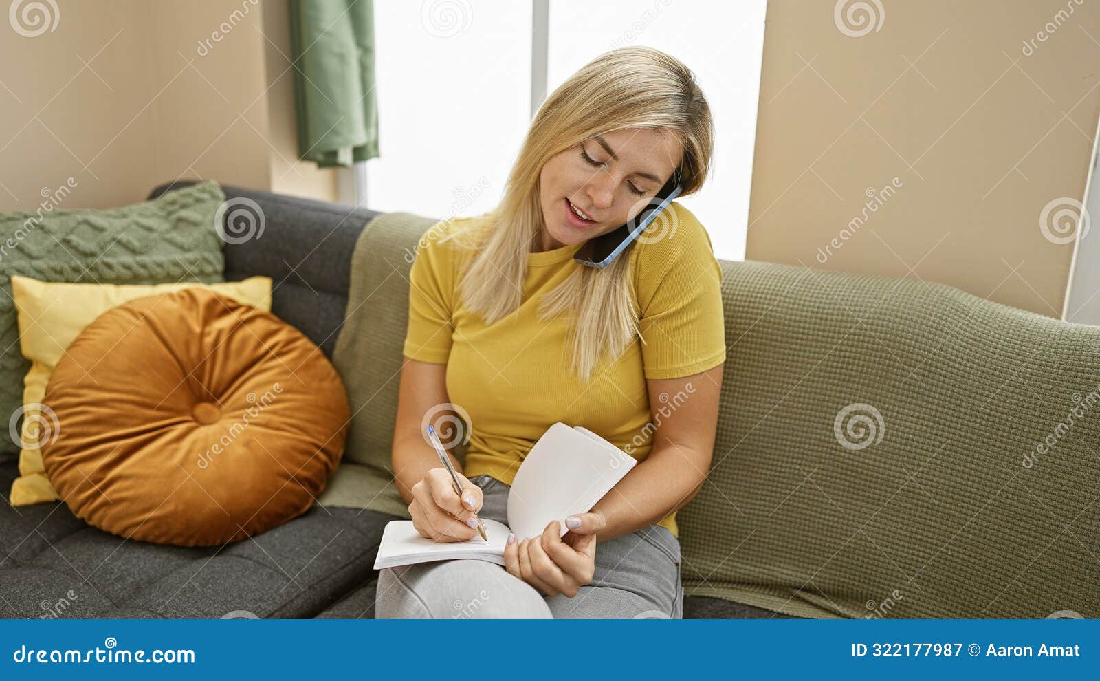 A Blonde Woman Multitasking at Home, Talking on the Phone while Writing ...