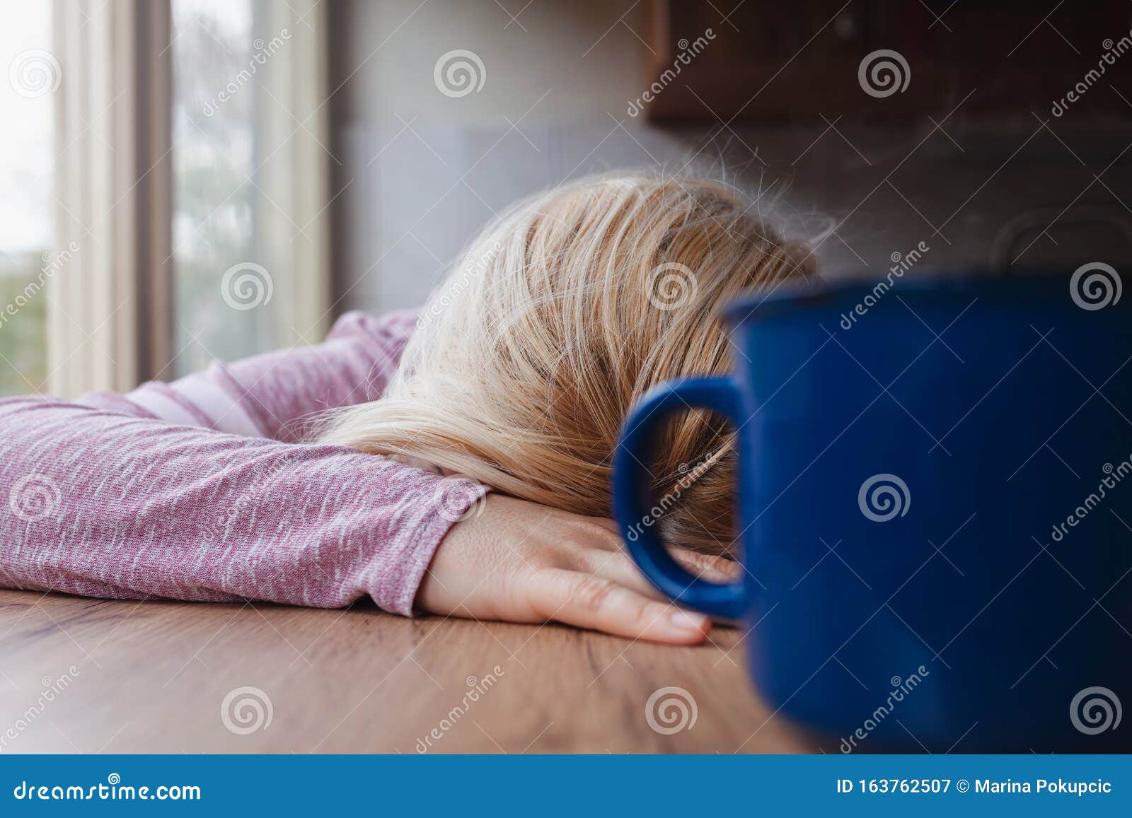 Blonde Woman Resting Her Head on a Kitchen Table Cup of Coffee in Front ...