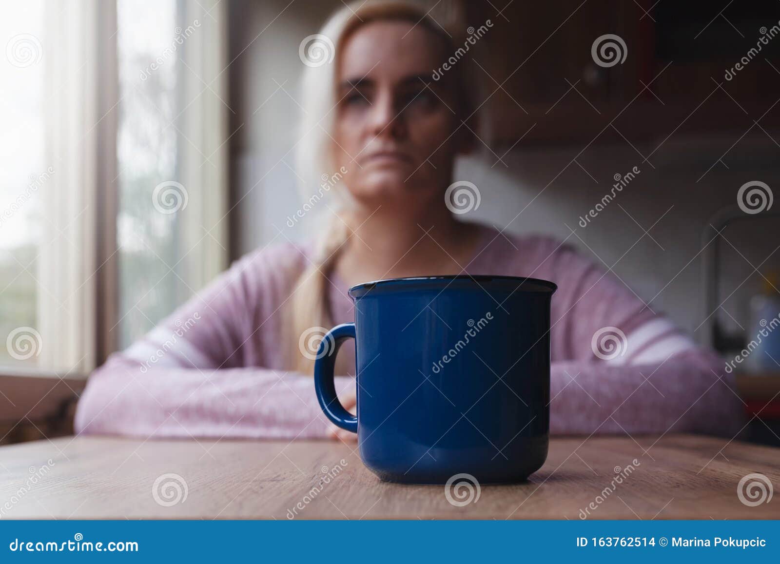 Blonde Woman Sitting at the Kitchen Table, Contemplating, with Cup of ...