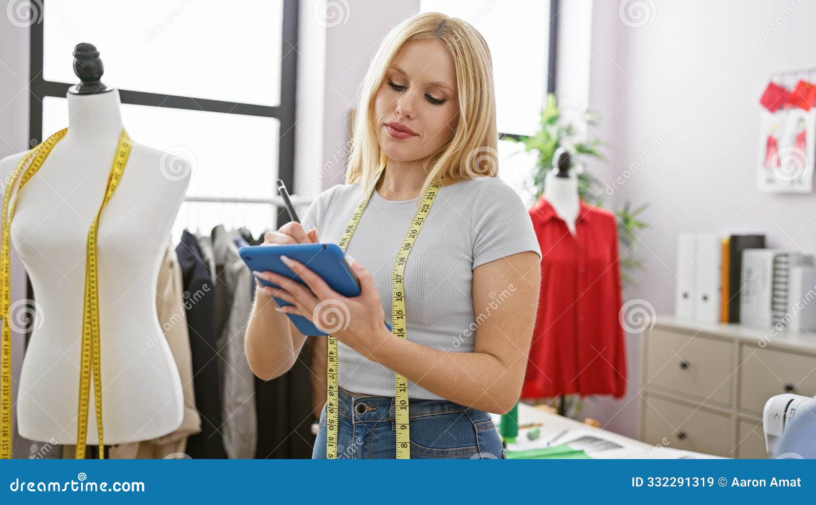 A Blonde Woman Tailor in a Workshop Measuring Mannequin Using a Tablet ...