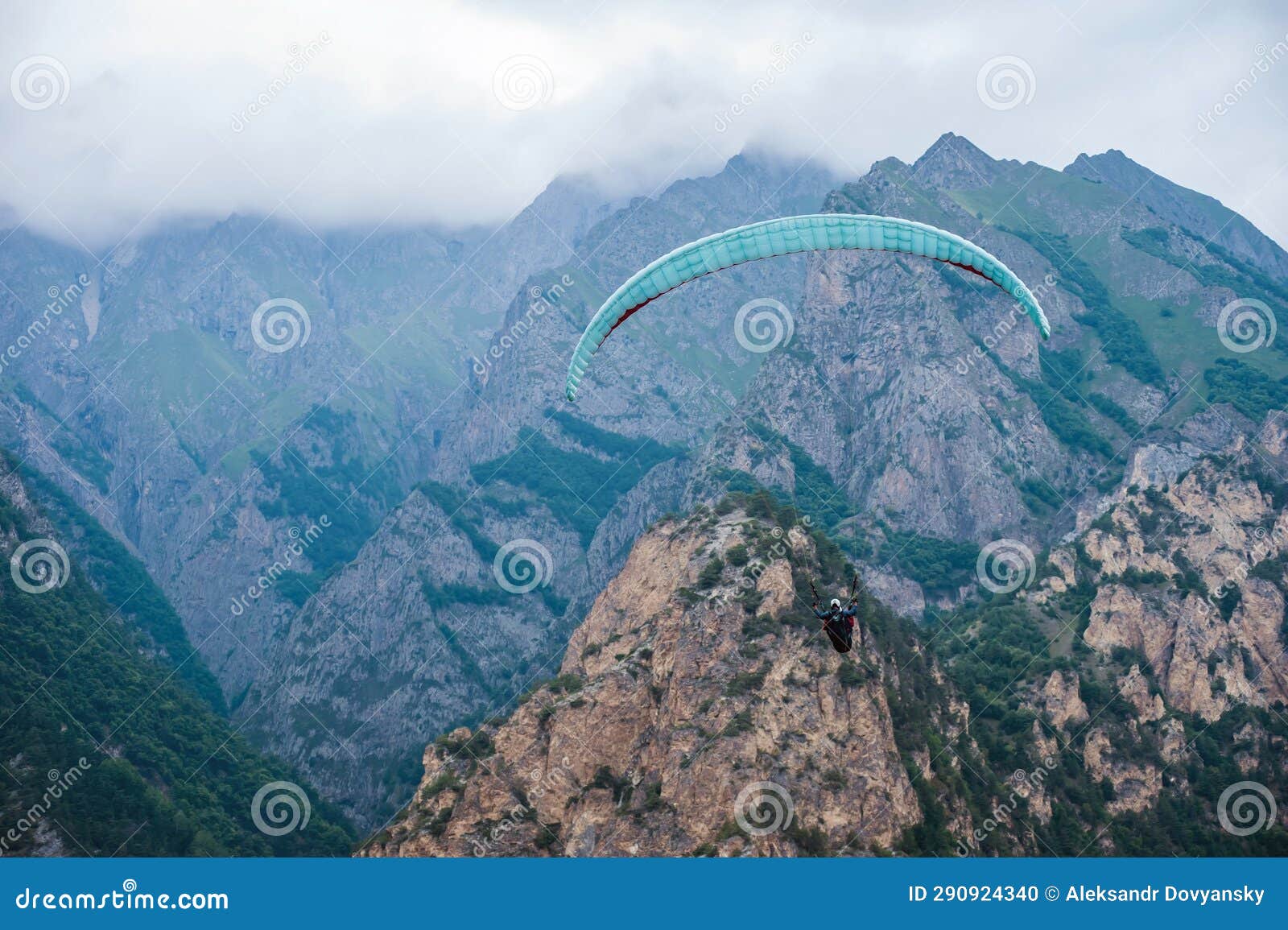 Blue Paraglider Flies Against a Background of Mountains and Clouds ...