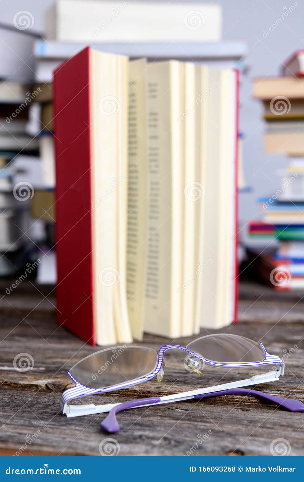 Book and Reading Glasses in Front of Piles of Different Books Stock ...