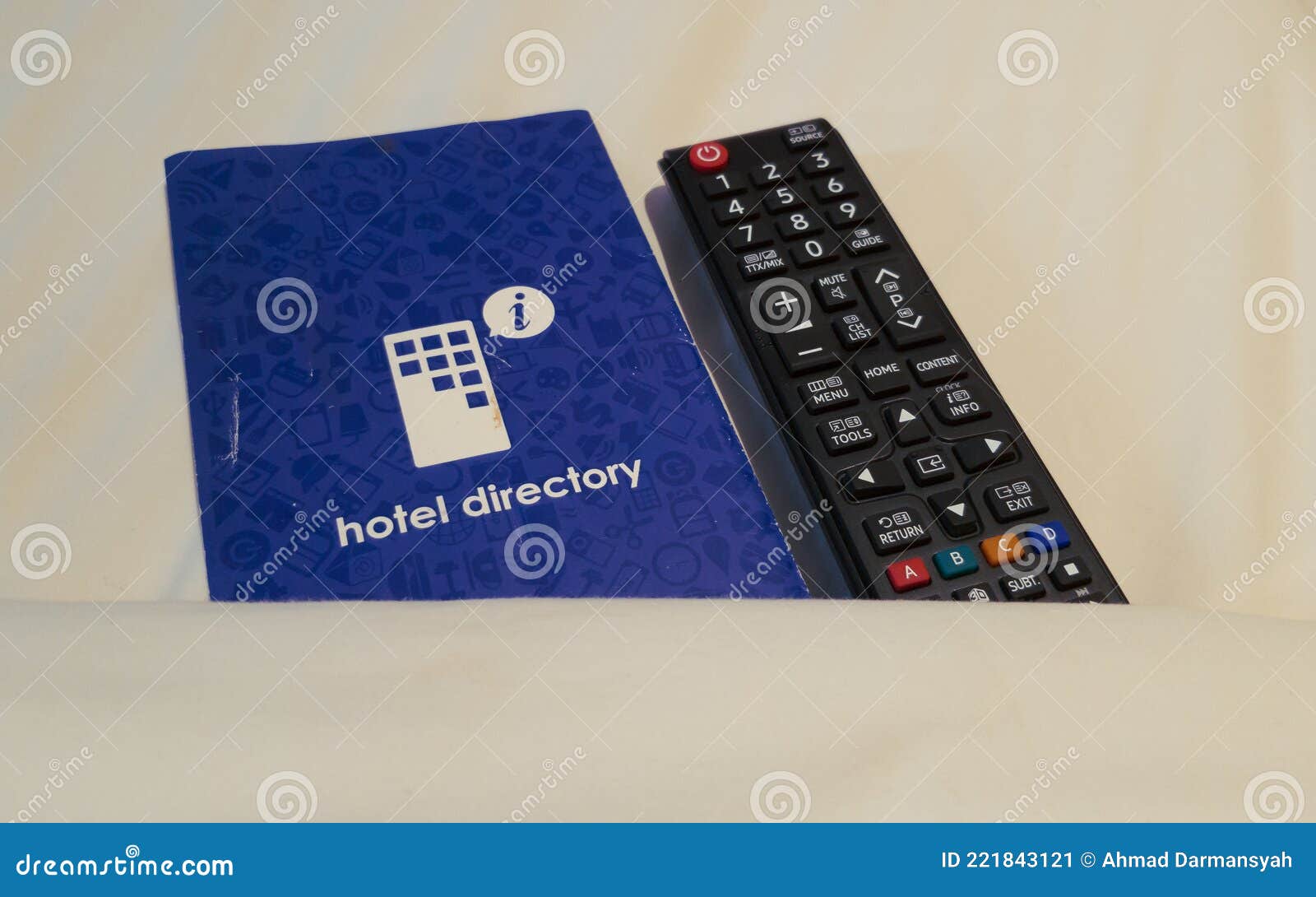 A Booklet of Hotel Directory and TV Remote on the White Bed Covered by ...