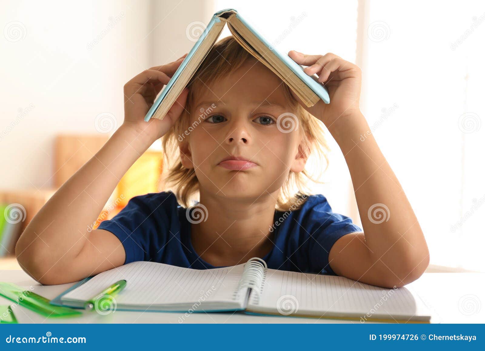 Bored Little Boy with Book on His Head Doing Homework at Table Indoors ...