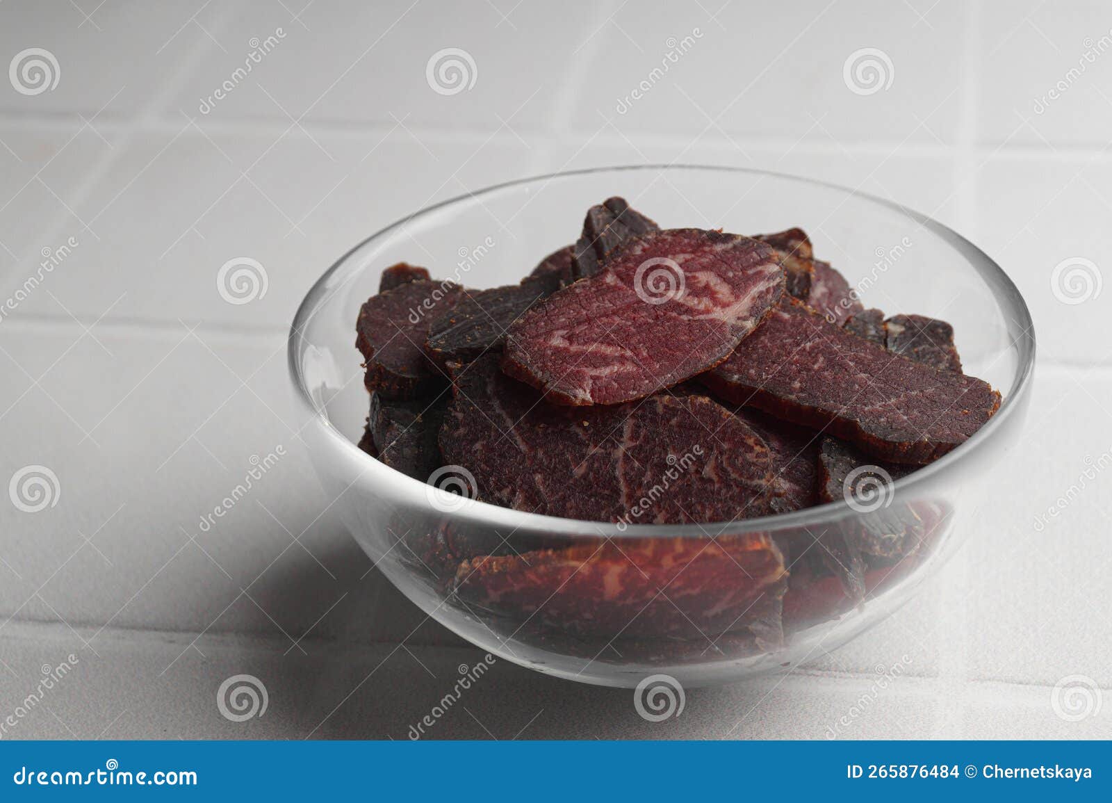 Bowl with Pieces of Delicious Beef Jerky on White Tiled Table, Closeup ...