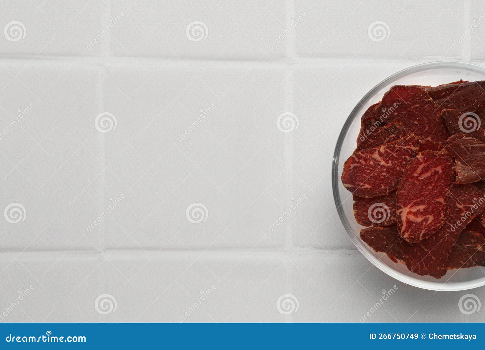 Bowl with Pieces of Delicious Beef Jerky on White Tiled Table, Top View ...