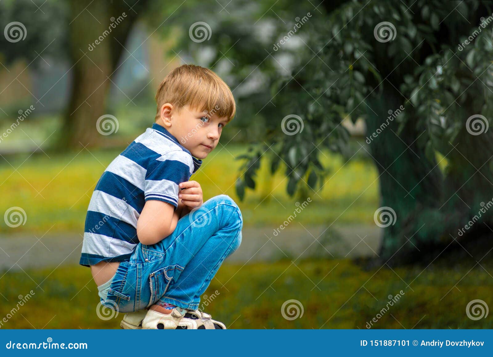 A Boy in Blue Jeans Squats in the Park Looking Around Stock Image ...