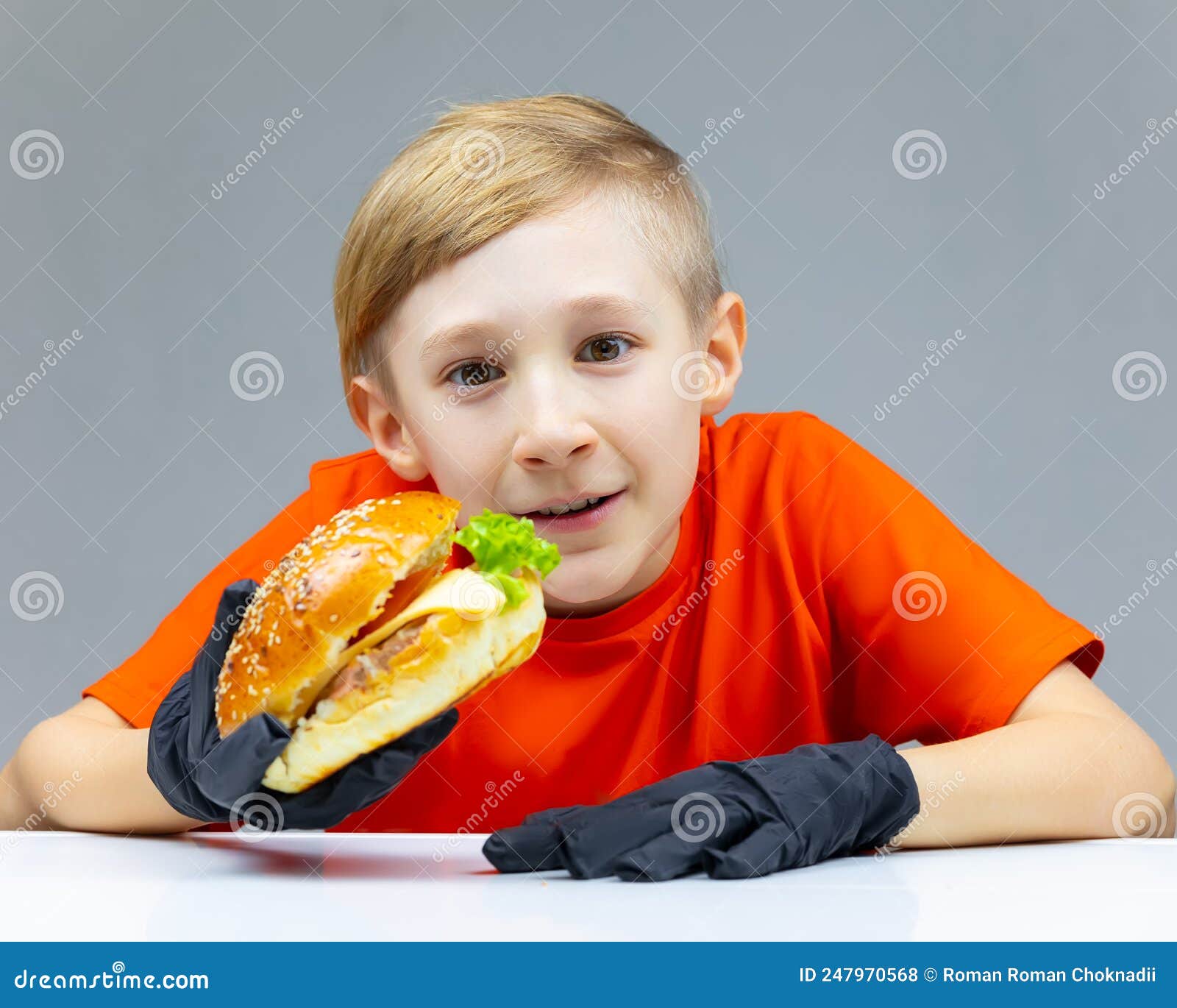 A Boy with a Cheeseburger Holds it in His Hand and Looks Straight Stock ...