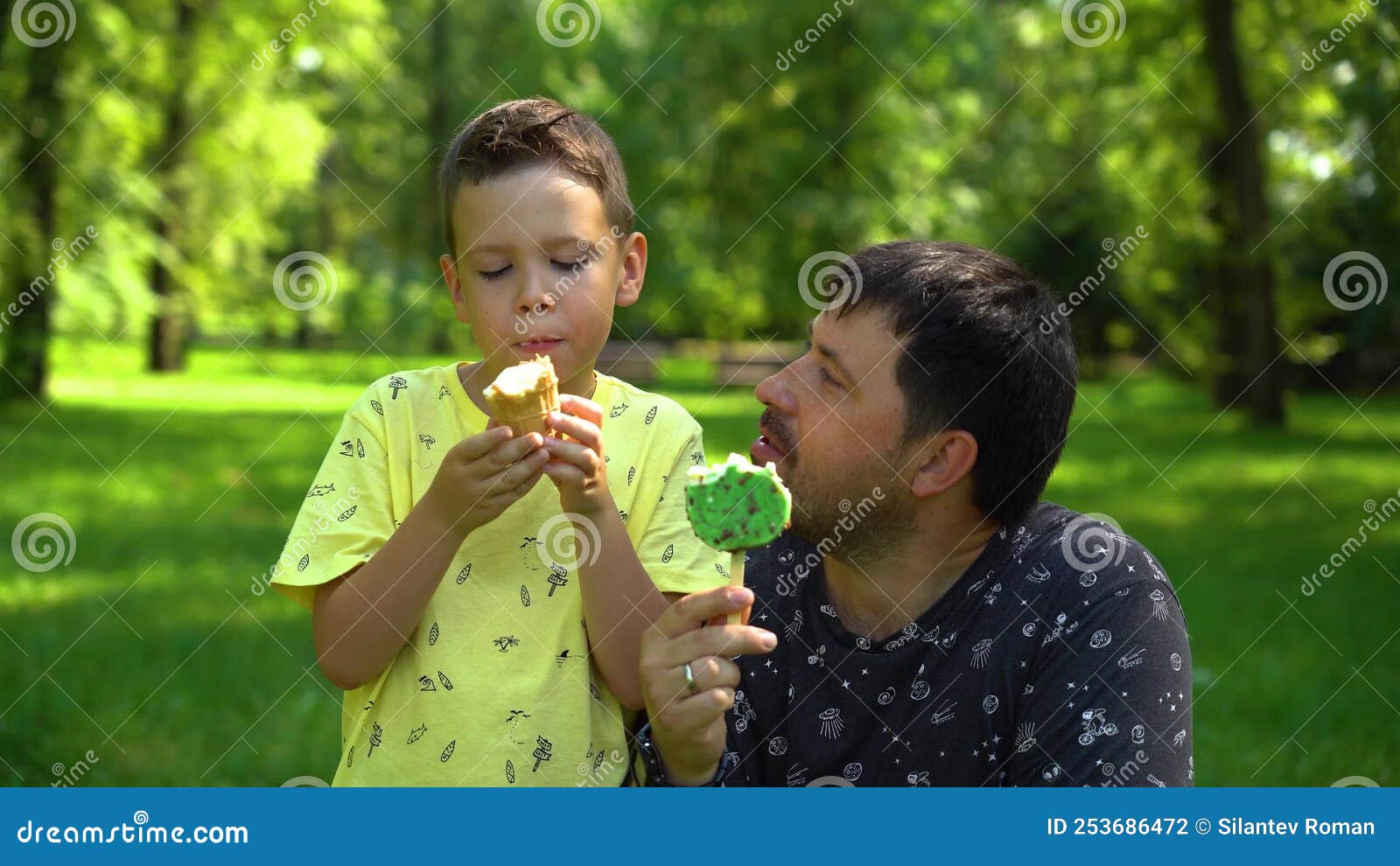 Father And Son Eat Ice Cream And Gesture Cool On A Sunny Summer Day In