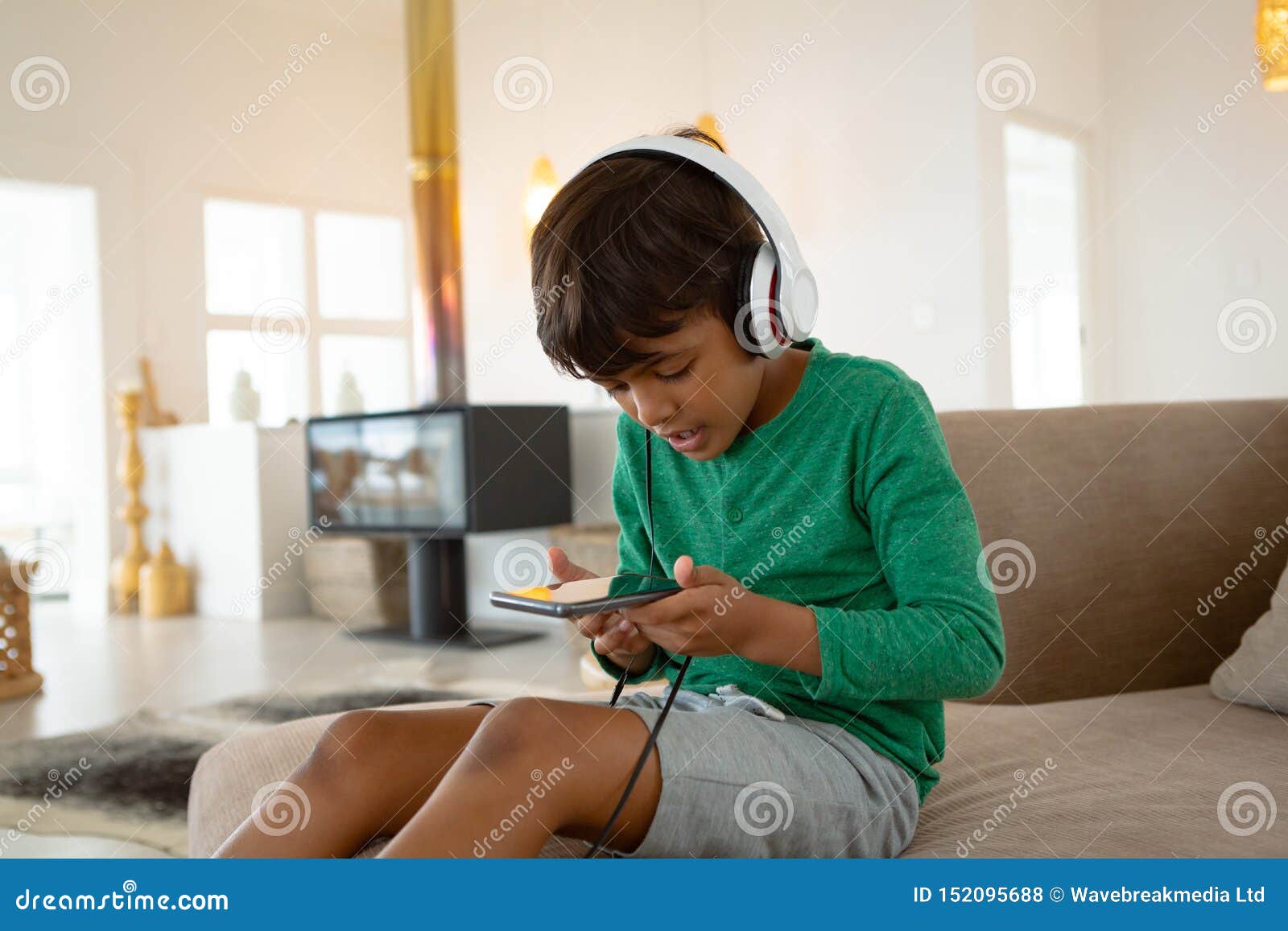 Boy with Headset Playing Game on Mobile Phone on Sofa in a Comfortable ...