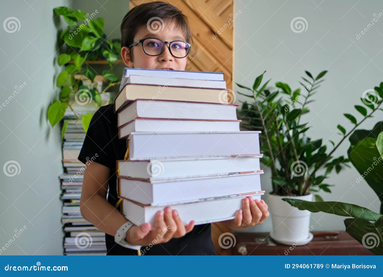 A Boy Holds a Stack of Books Against the Background Home Library. Stock ...