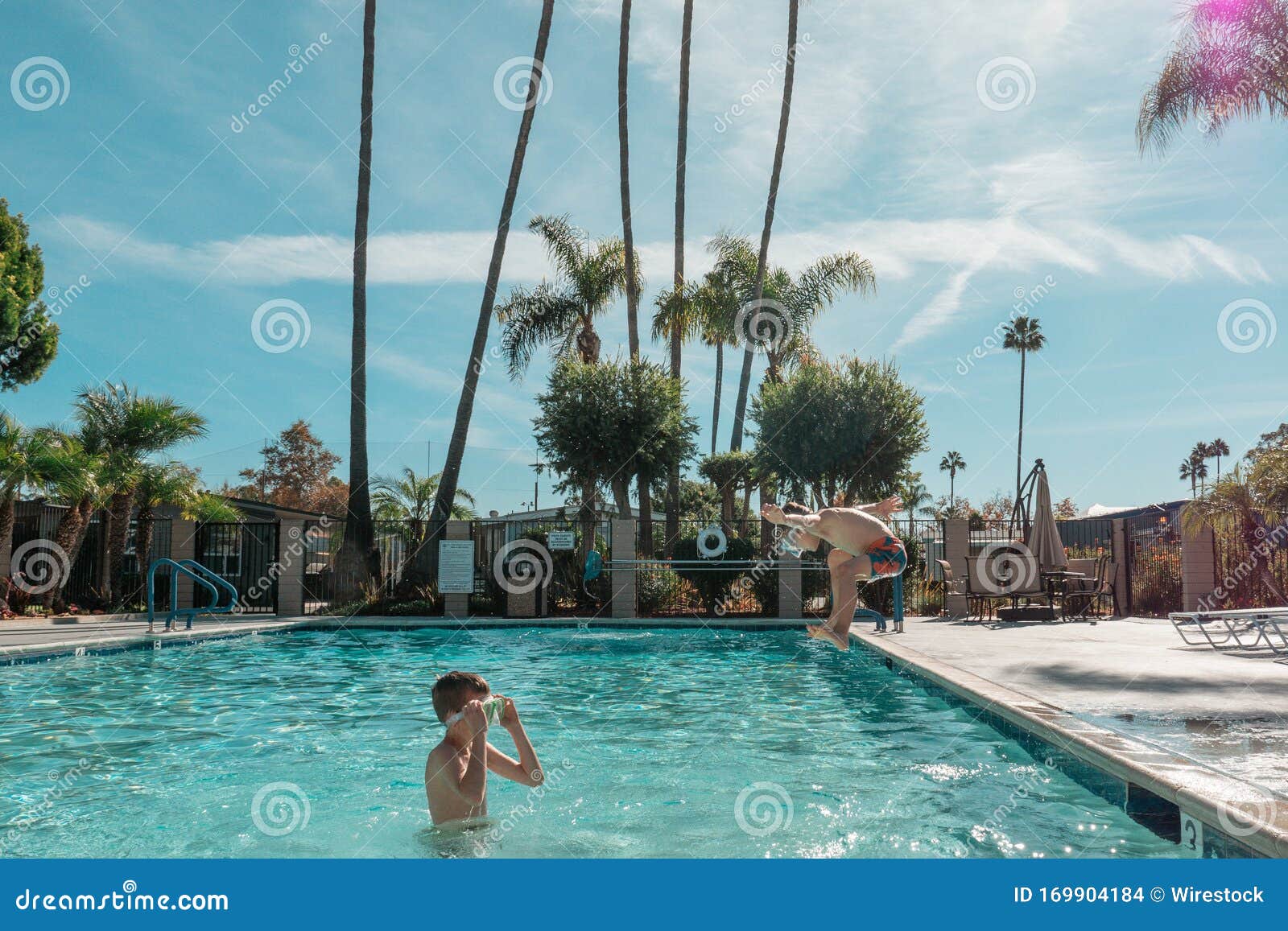 Boy Jumping into the Pool Surrounded by Palms Under a Blue Sky and ...
