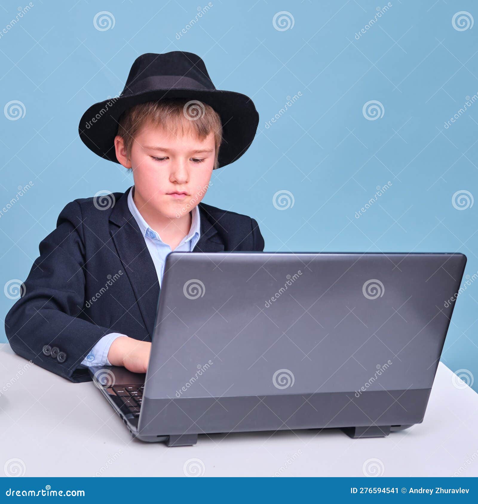 A Boy in a School Suit and a Black Hat at a Computer during Distance Le ...