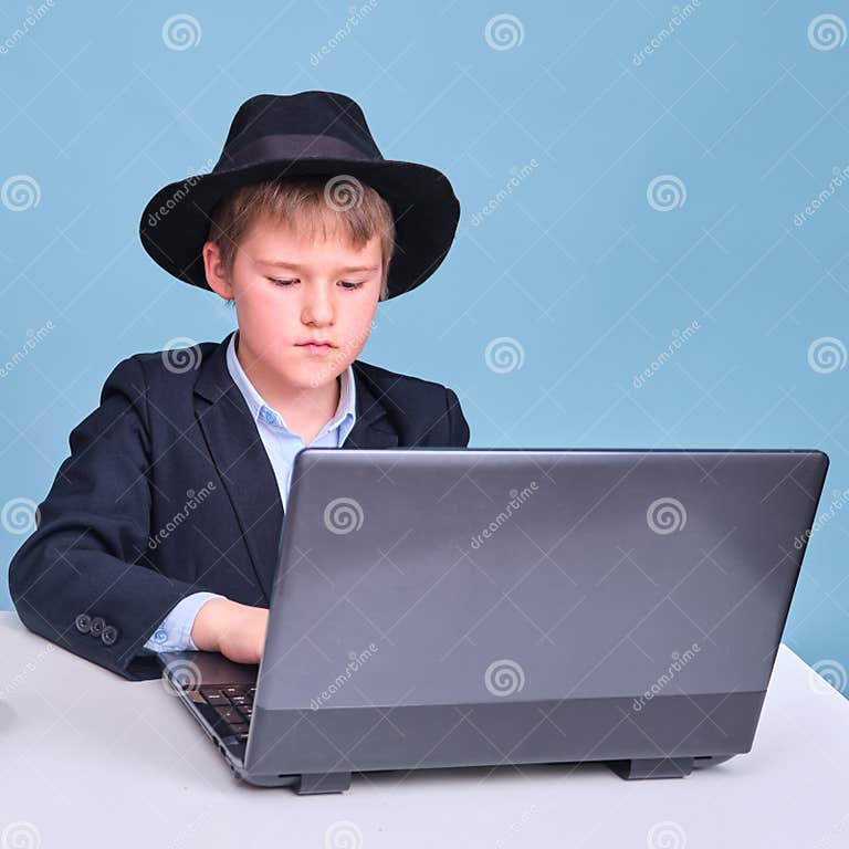A Boy in a School Suit and a Black Hat at a Computer during Distance Le ...
