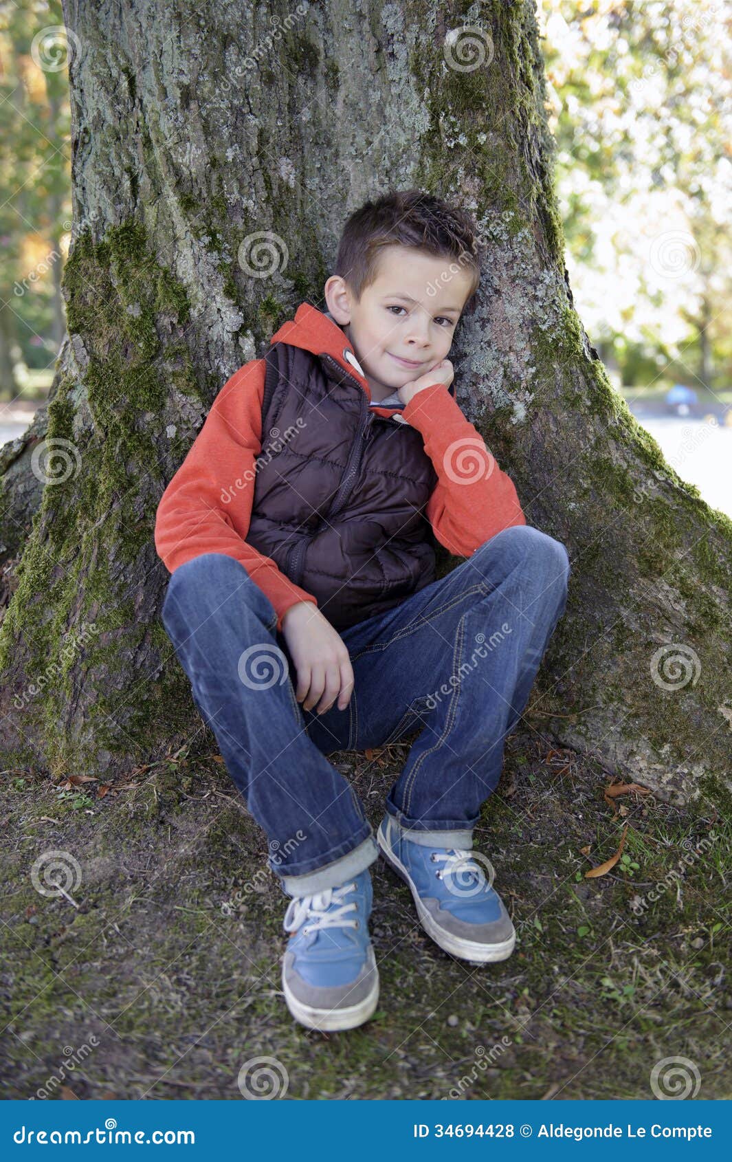 Boy seated against a tree stock photo. Image of acreage - 34694428