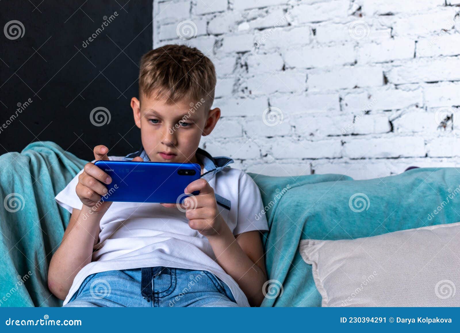 Boy Sits on the Sofa in the Room and Uses the Phone To Play Stock Image ...