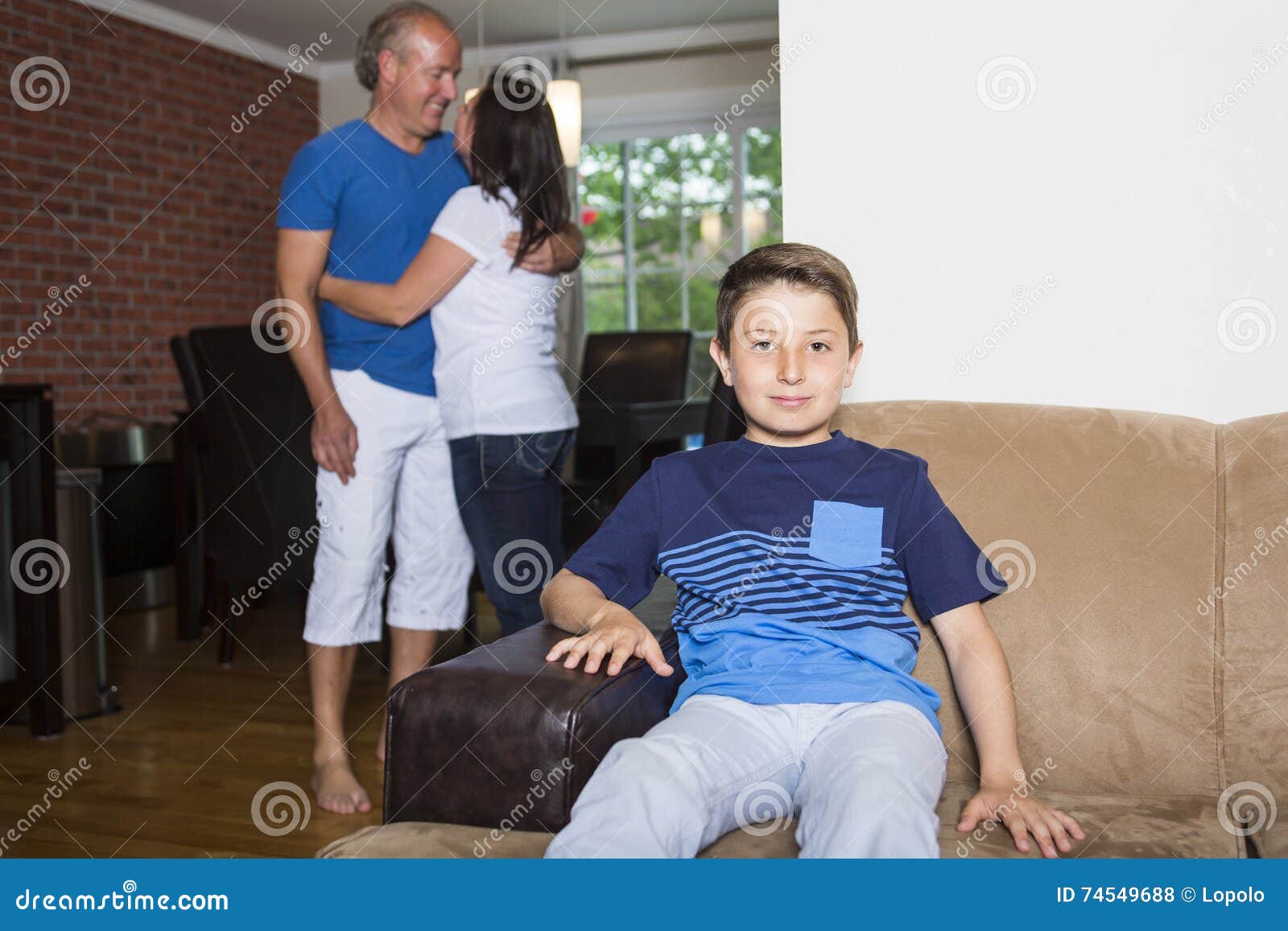 Boy Sitting in Couch at Home, Parents in Background Stock Photo - Image ...