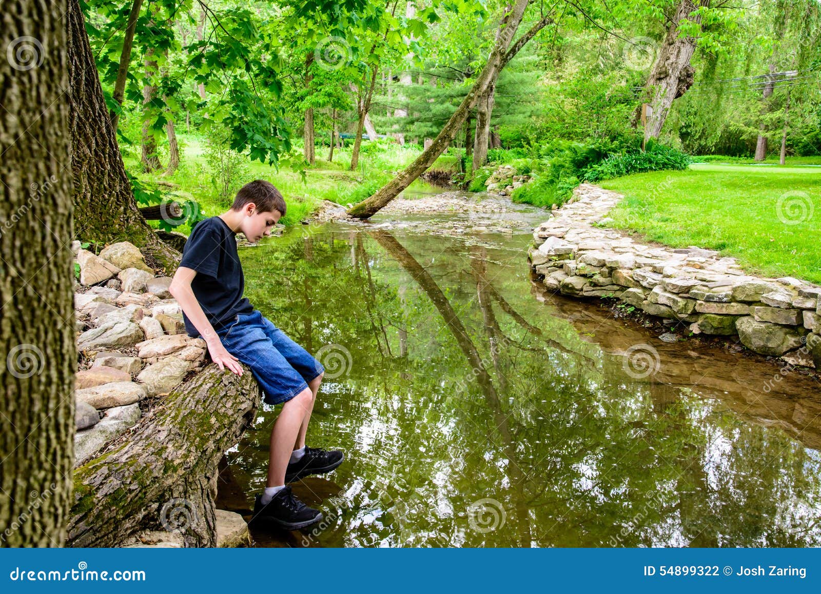 Boy Sitting at Edge of Stream Getting Shoes Wet Stock Photo - Image of ...