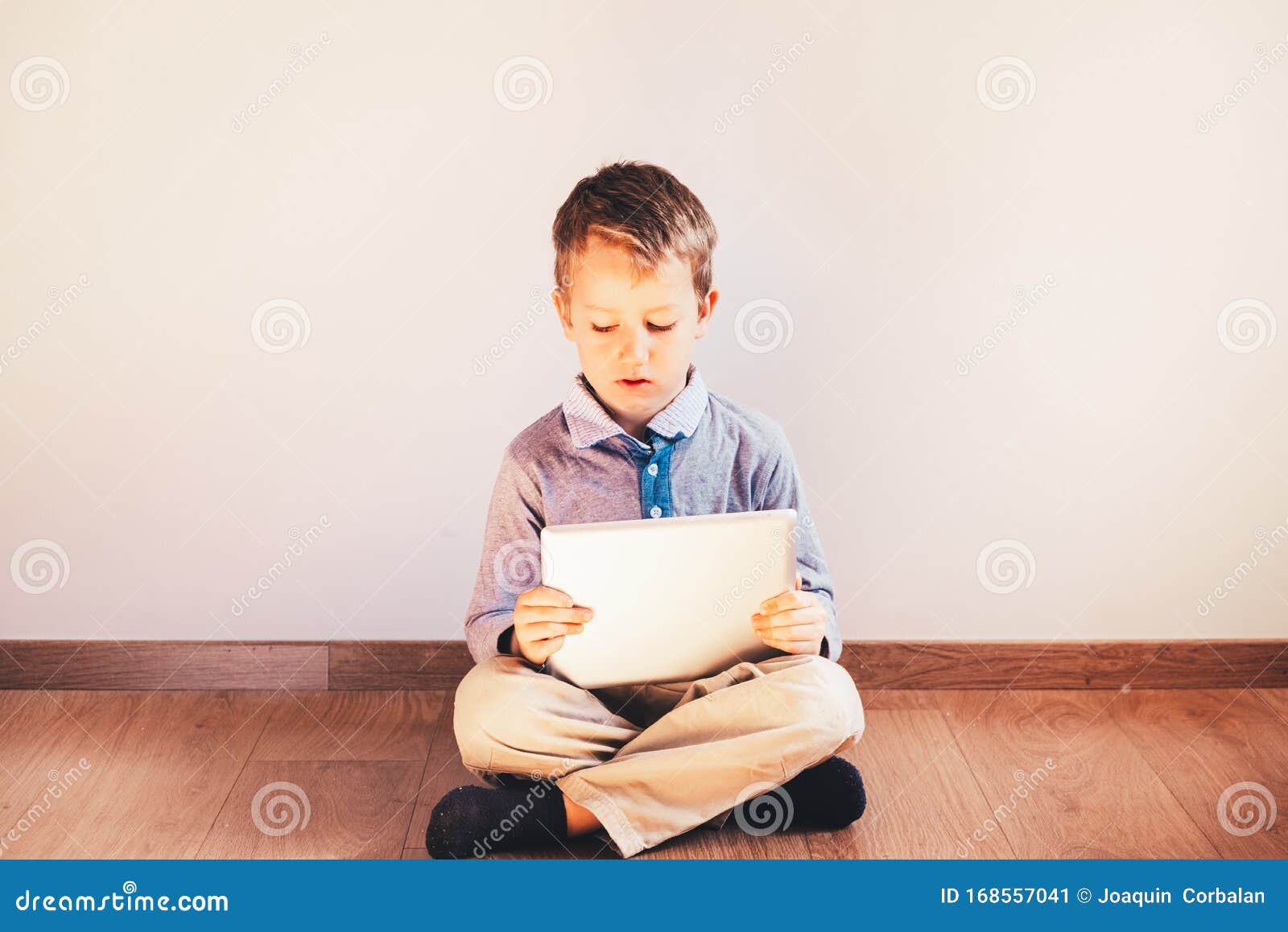 Boy Sitting on the Floor with a Digital Tablet in His Hands, Using it ...