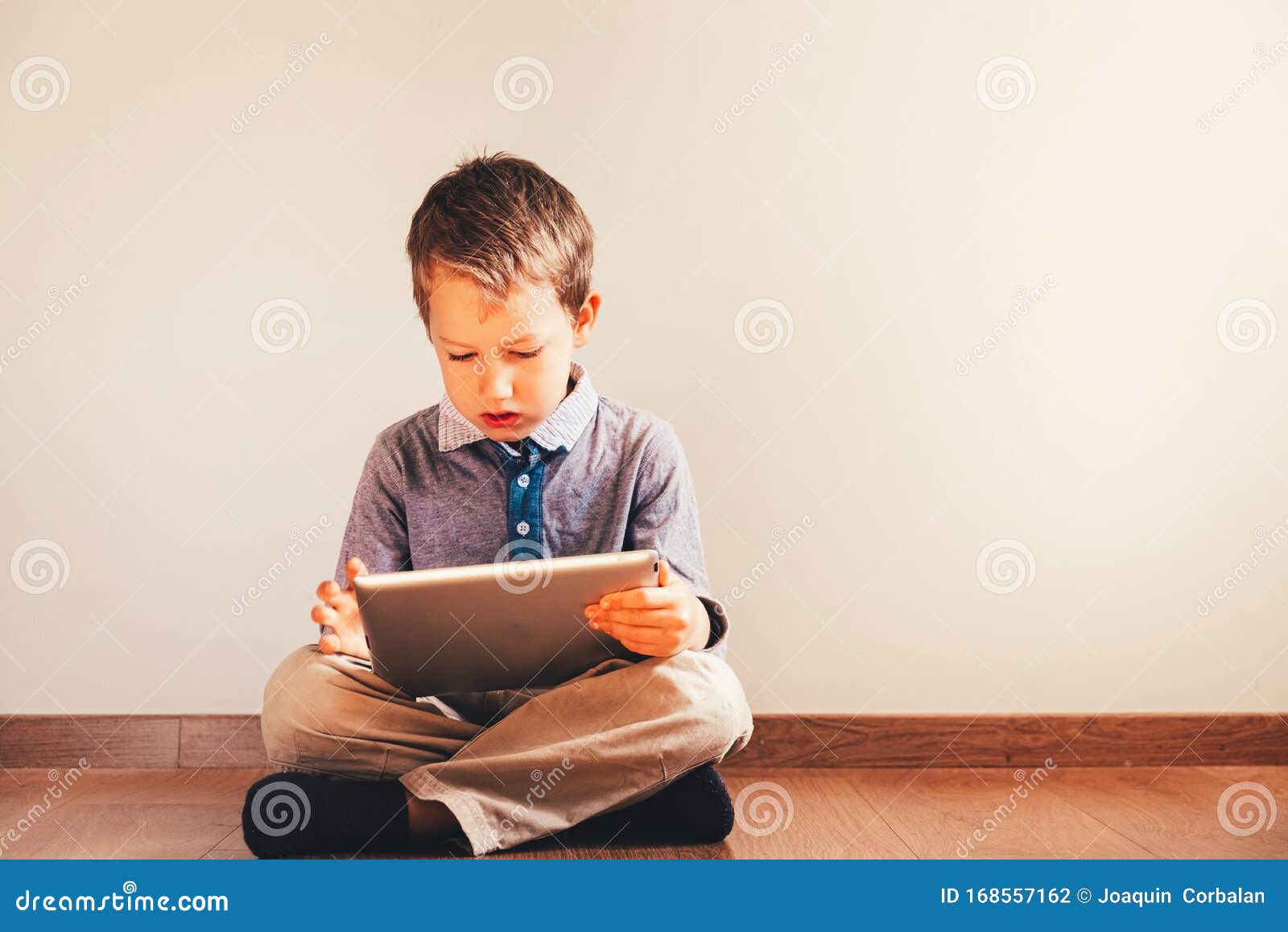 Boy Sitting on the Floor with a Digital Tablet in His Hands, Using it ...