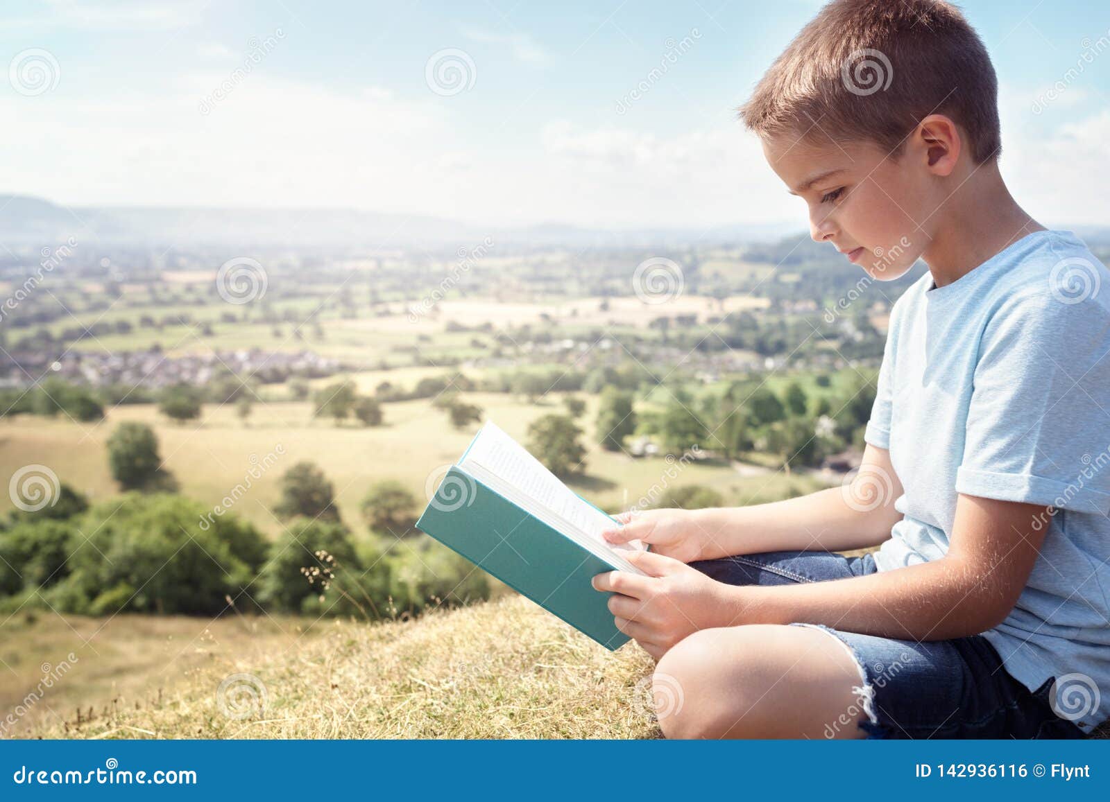 Boy Sitting on a Hill Reading a Book in a Meadow Stock Photo - Image of ...