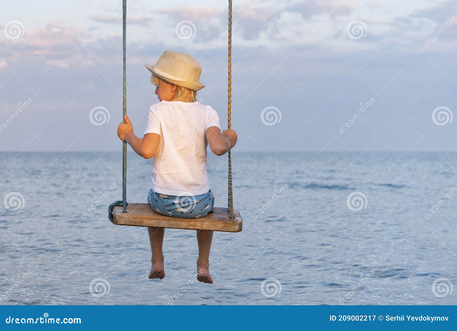 Boy in Straw Hat Sitting on a Rope Swing on Sea Background. Back View ...