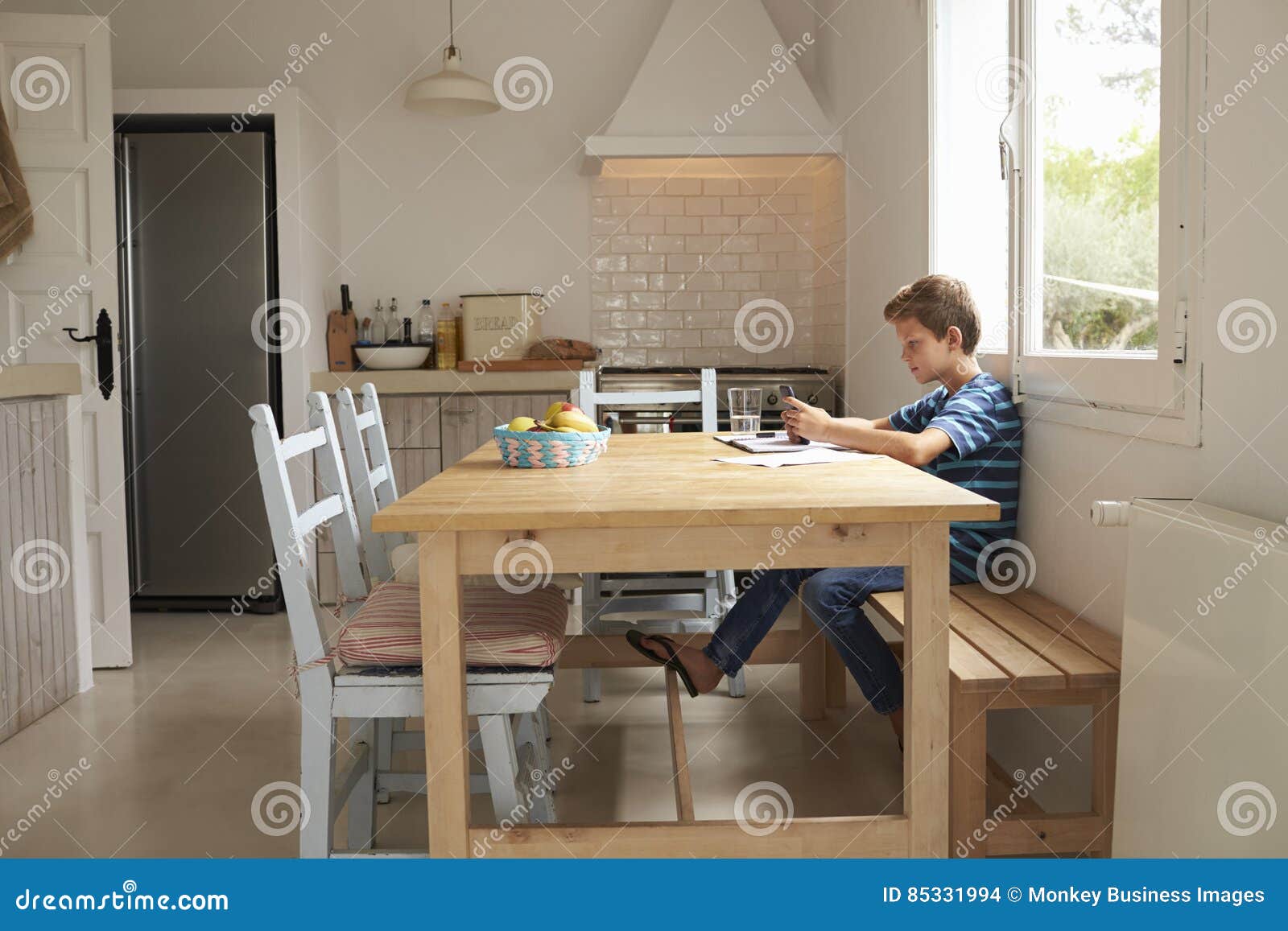 Boy Uses Mobile Phone Whilst Doing Homework at Kitchen Table Stock ...