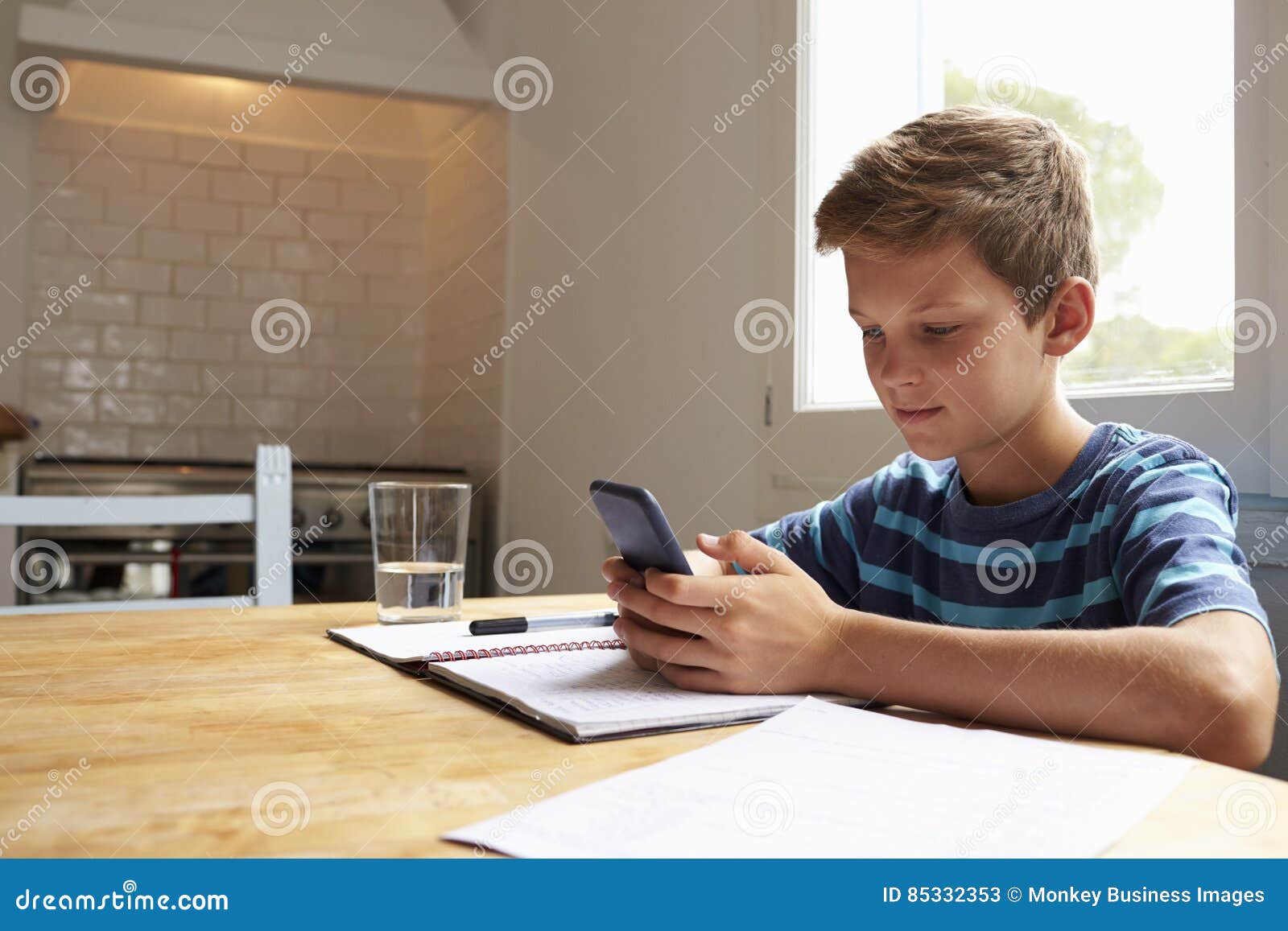 Boy Uses Mobile Phone Whilst Doing Homework at Kitchen Table Stock ...