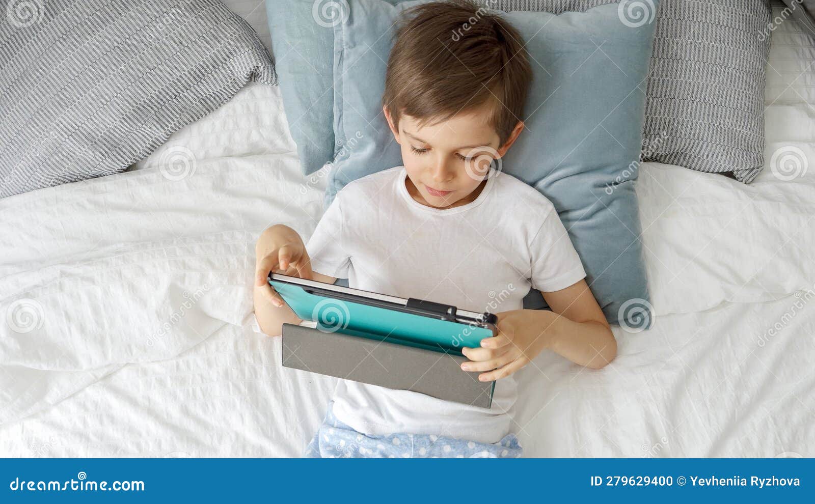 A Boy Using a Tablet Computer while Lying in Bed during the Day. His ...