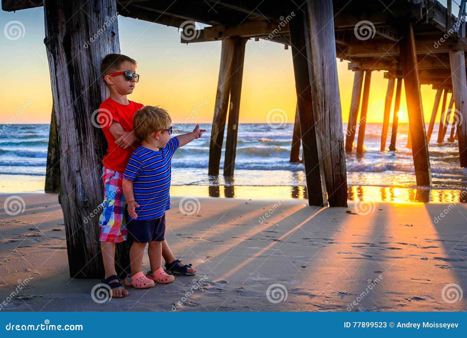 Boys Standing on the Beach Under Pier at Sunset Stock Image - Image of ...