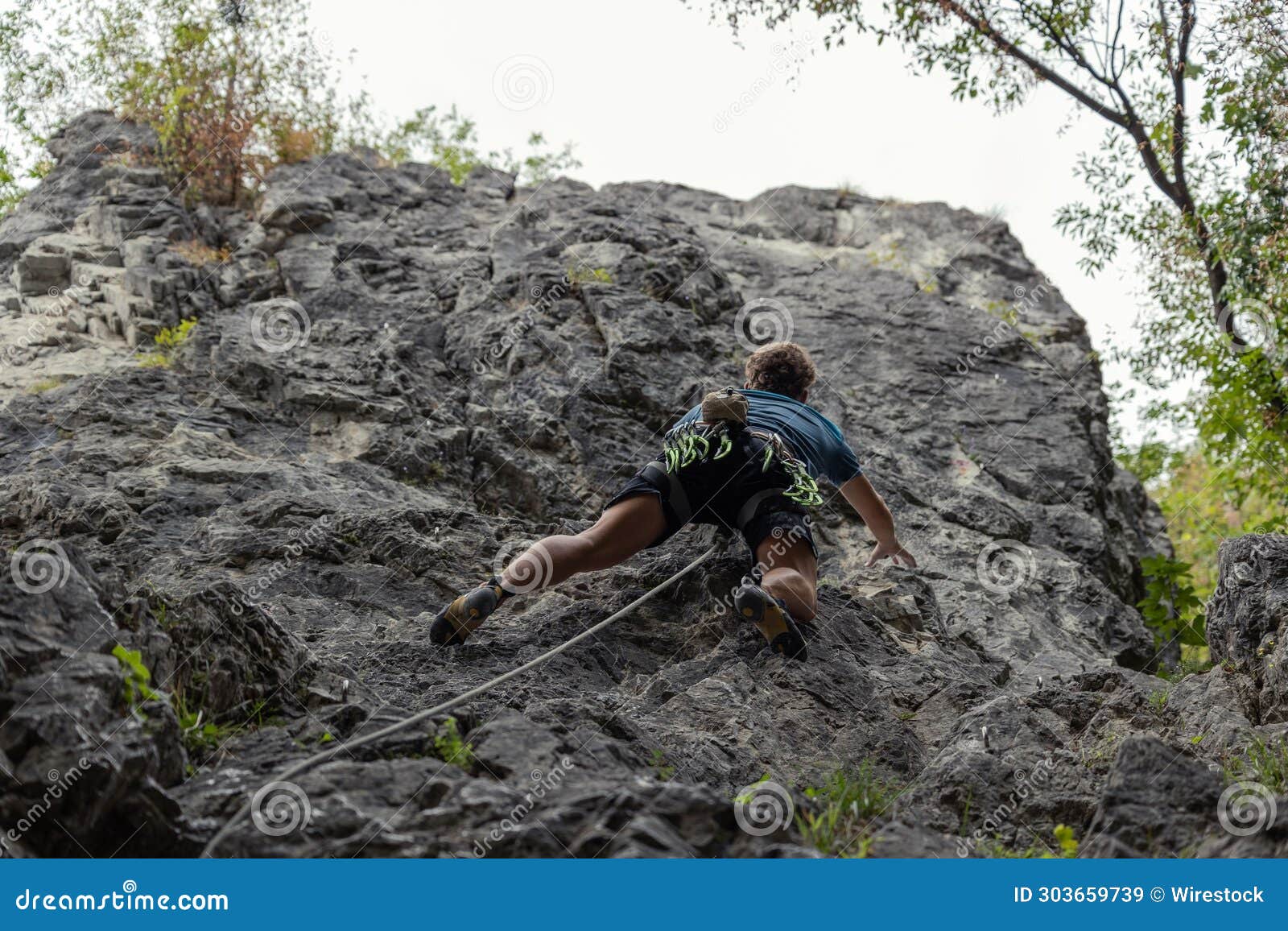 Brave Climber Scaling a Towering Cliff Face in a Lush Green Forest ...