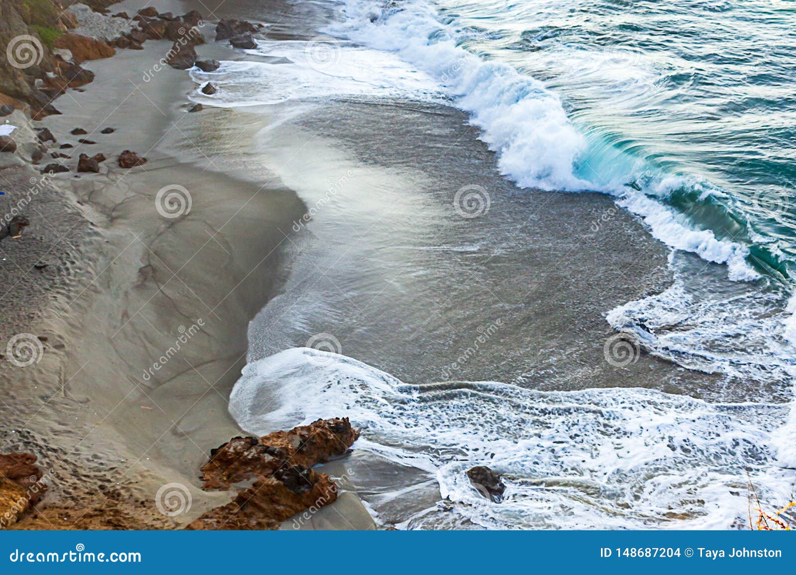 Breaking Tourqoise Wave on Dark Sandy Beack with Foam Trails and Rocks ...