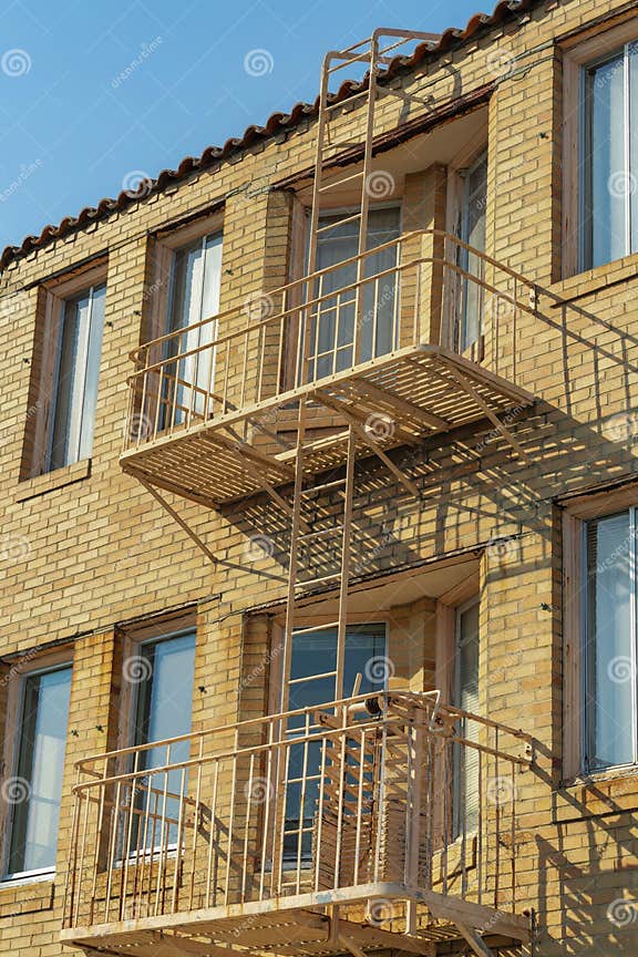 Brick Building Facade with Brown Fire Escape Ladders and Platforms with Large Windows and Blue ...