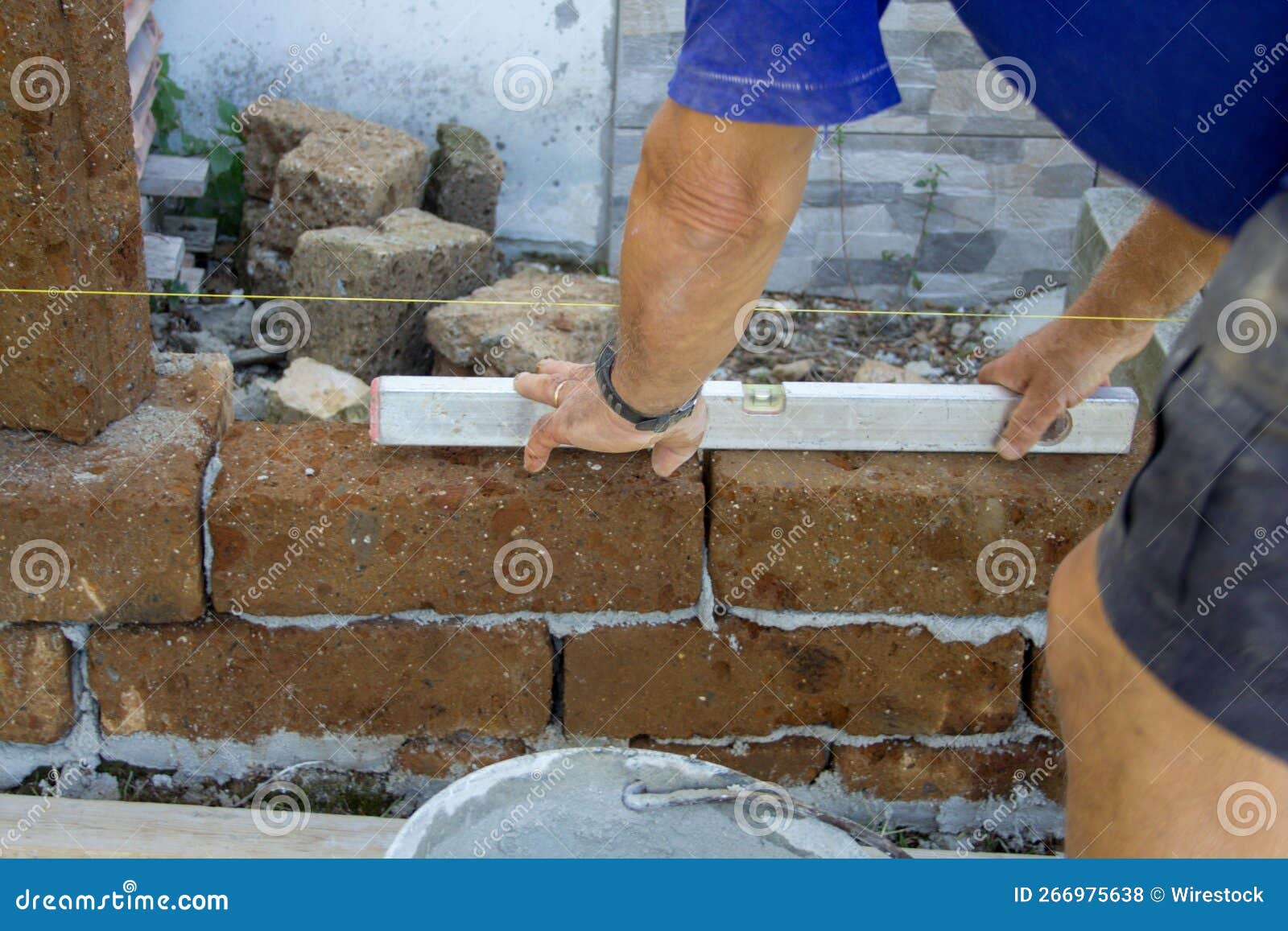 Bricklayer with Level Checks the Plan of a Low Wall that he Builds ...