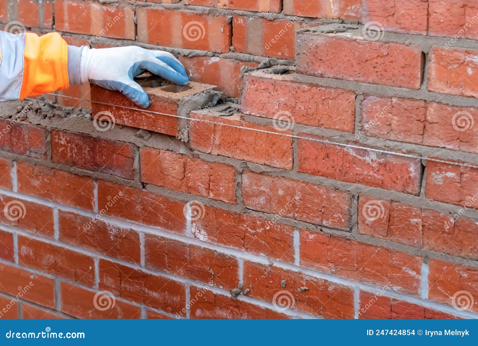 Bricklayer in Safety Vest and a Helmet Laying a Brick Wall Using a ...