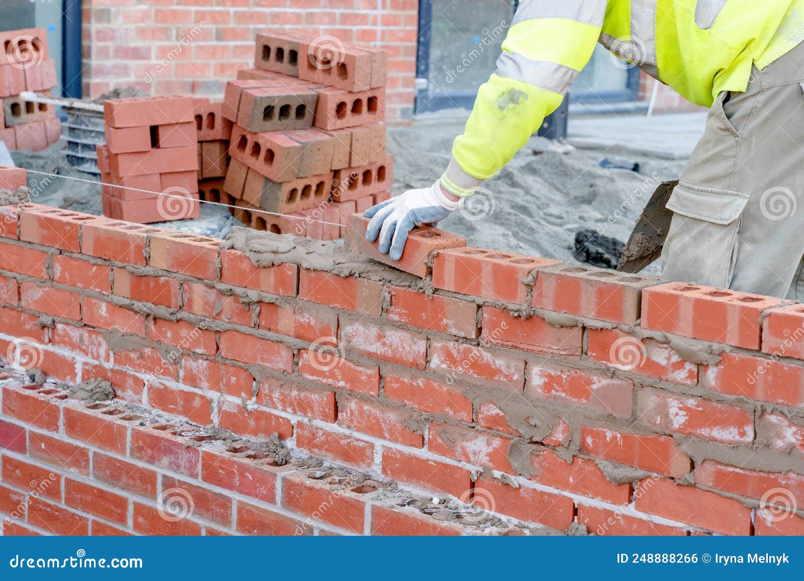 Bricklayer in Safety Vest and Helmet Laying a Brick Wall Using a Trowel ...