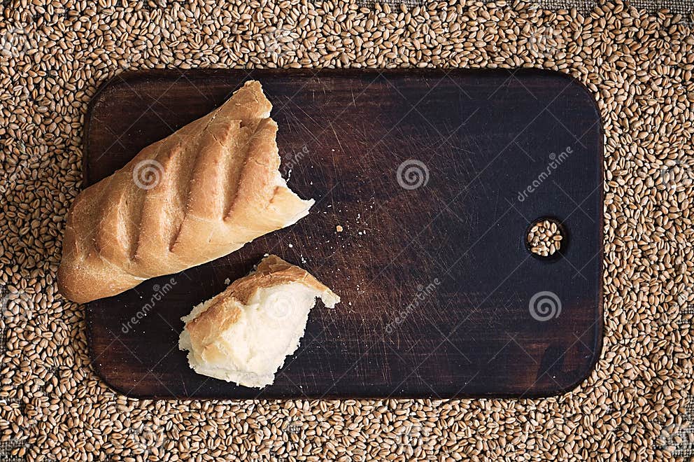 Broken Bread on a Kitchen Board Against a Background of Wheat Grains ...
