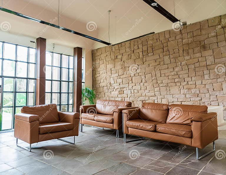 Brown Sofas Against Stone Tiles Cladding Wall in Room with High Ceiling ...