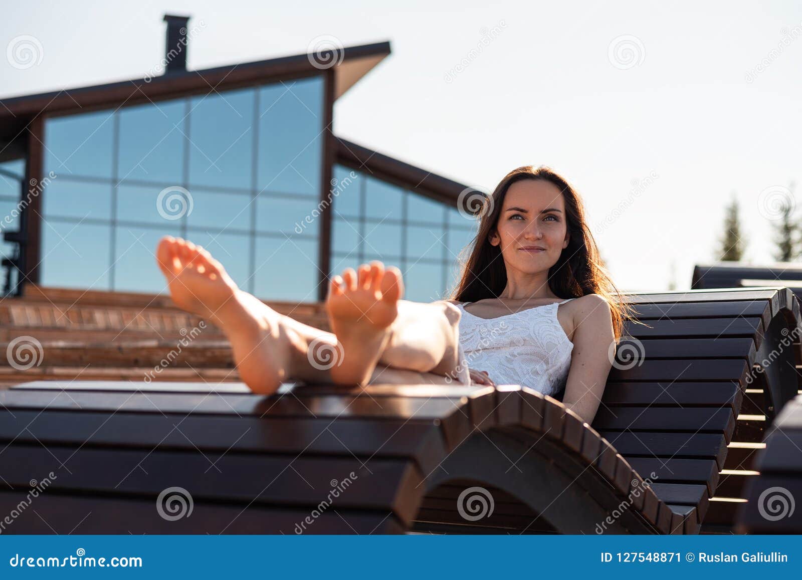 Brunette Girl Lying On A Wooden Lounger Barefoot And Smiling Stock