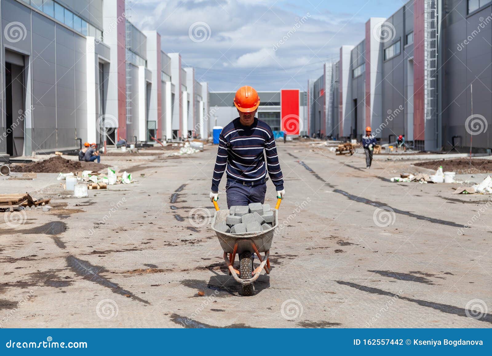 Builder Carrying Wheelbarrow with Concrete on the Construction Site ...