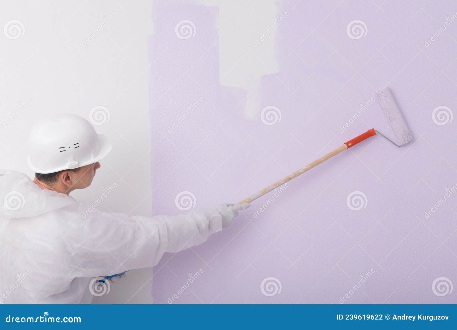 A Builder in Protective Clothing and a Helmet, Paints the Wall with a ...