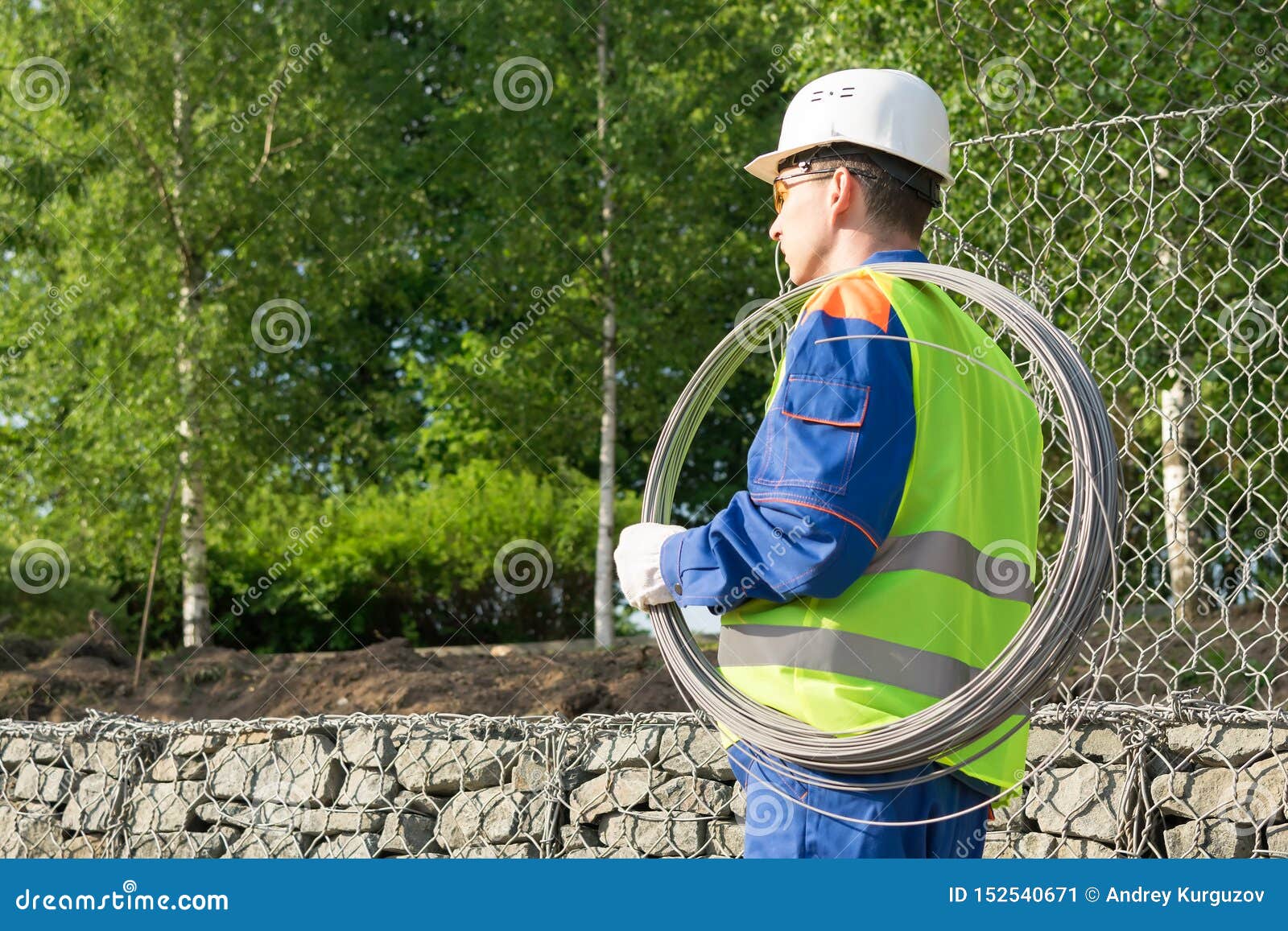 Builder in a White Helmet Carries a Hank of Wire on His Shoulder, Rear ...