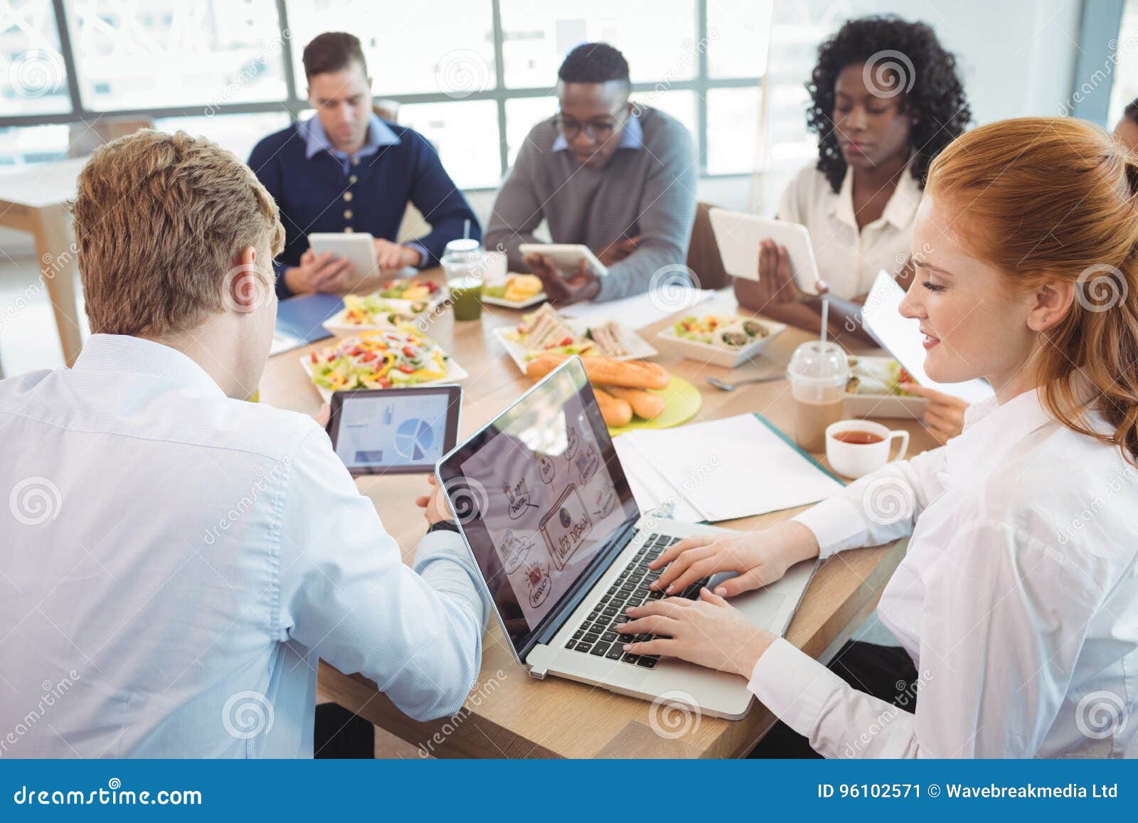 Business Colleagues Using Laptop and Digital Tablets Around Breakfast ...