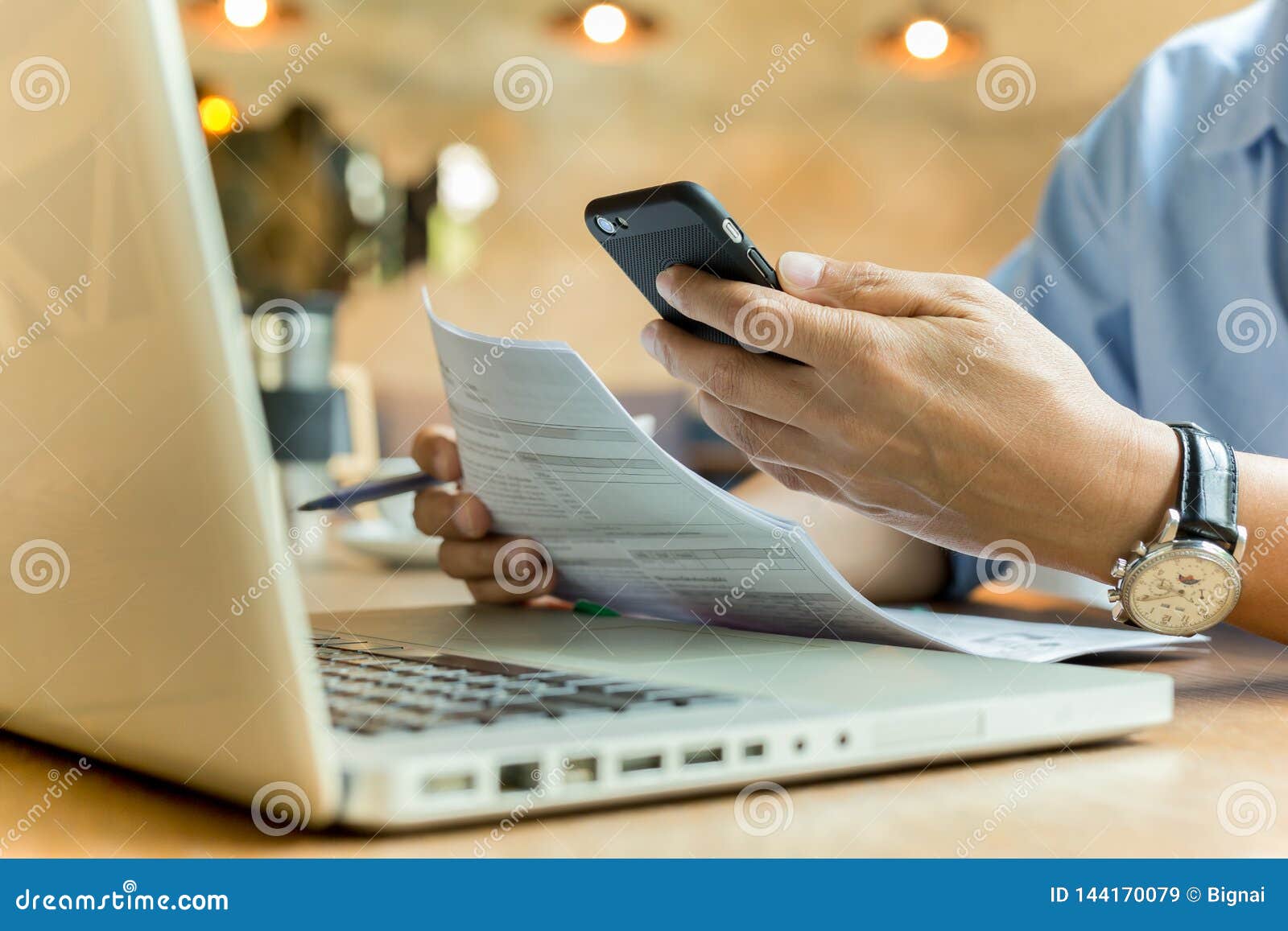 Business Man Using Cell Phone and Holding Document with Laptop on Table ...